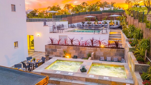 Uma área de piscina no terraço com espreguiçadeiras, uma banheira de hidromassagem e uma escadaria que leva a um terraço.