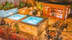 Uma área de spa com duas banheiras de hidromassagem, uma sauna de madeira e uma mesa de jantar com cadeiras.