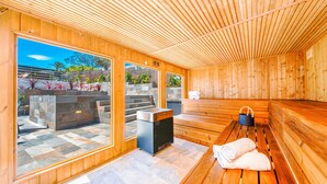 Uma sala de sauna com paredes de madeira, um banco de pedra, um aquecedor de sauna e vista para um jardim.