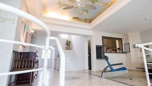 Amplo interior com escada para um andar superior, ventilador de teto e área de estar com uma cadeira azul.