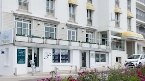Um hotel com fachada branca, várias varandas com toldos amarelos e uma entrada visível com uma placa.