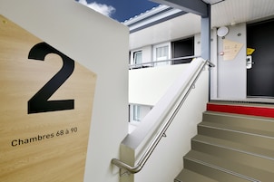 Uma escadaria com corrimão, uma porta de madeira com o número 2, e uma placa indicando quartos de 68 a 90.