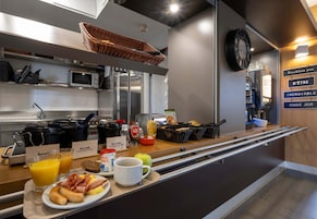 Um balcão de café da manhã com diversas opções de alimentos, incluindo torradas, ovos, bacon e frutas. Também há dois copos de suco de laranja e uma xícara de café.
