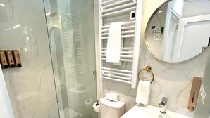 Uma casa de banho moderna com cabine de chuveiro em vidro, sanita, lavatório com espelho e barra de toalhas.