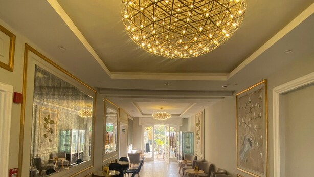Um amplo hall de hotel com um lustre central, áreas de estar e obras de arte emolduradas nas paredes.