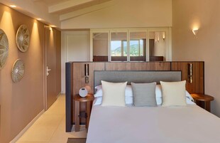 Quarto de hotel moderno com uma cama grande, cabeceira de madeira, mesa de cabeceira com abajur e arte decorativa na parede.