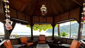 Uma área de estar coberta ao ar livre, com móveis de madeira e vista para o mar.