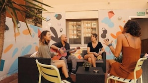 Um grupo de pessoas sentadas em móveis de exterior num pátio com um mural colorido na parede.