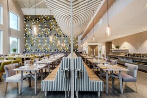 Um restaurante moderno com mesas comunitárias compridas, pé-direito alto e paredes com padrão geométrico.