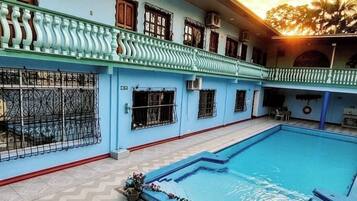 Piscina com deck revestido, rodeada por um edifício com várias janelas e uma varanda.