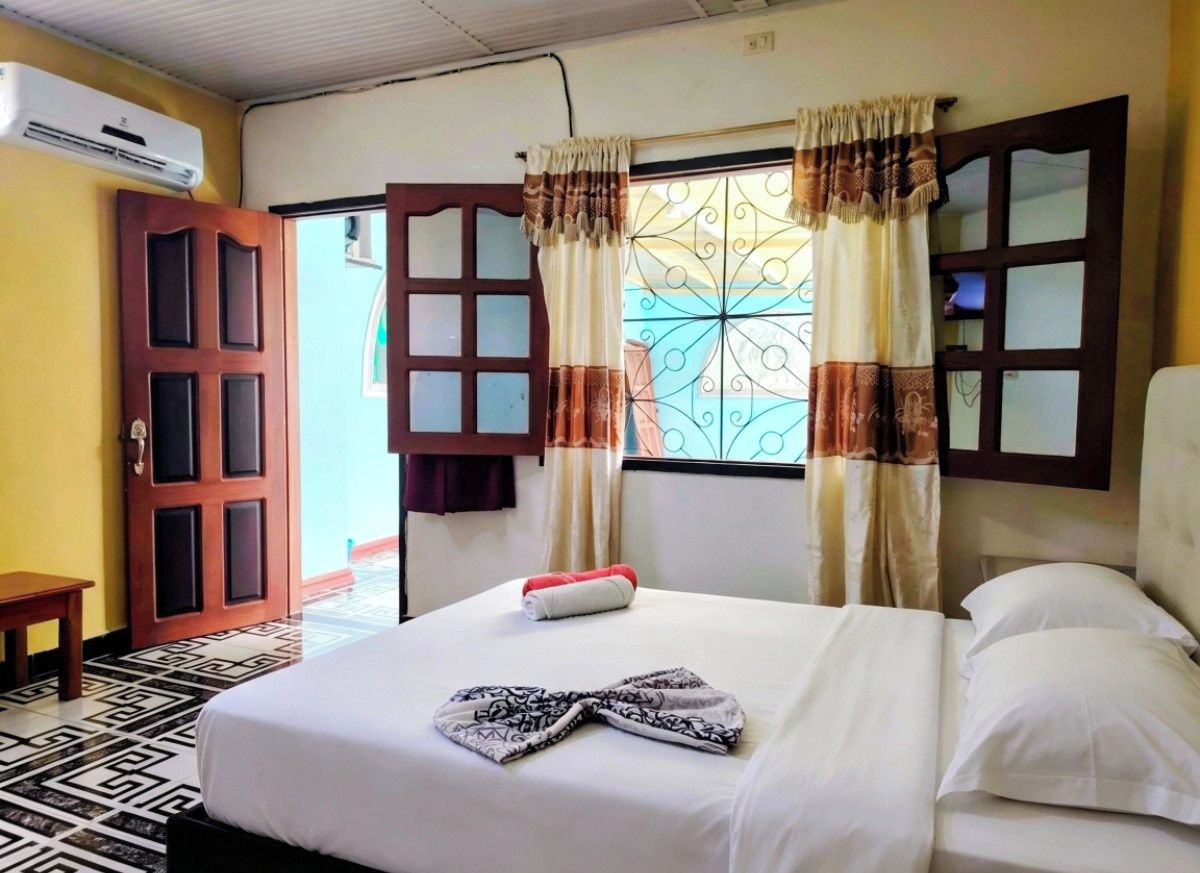 Quarto de hotel com cama, janela com cortinas, porta e aparelho de ar condicionado.