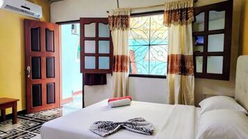 Quarto de hotel com cama, janela com cortinas, porta e aparelho de ar condicionado.