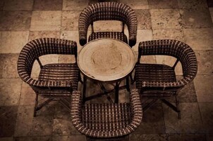 Uma mesa de vime com quatro cadeiras, posicionada no centro de um chão ladrilhado.