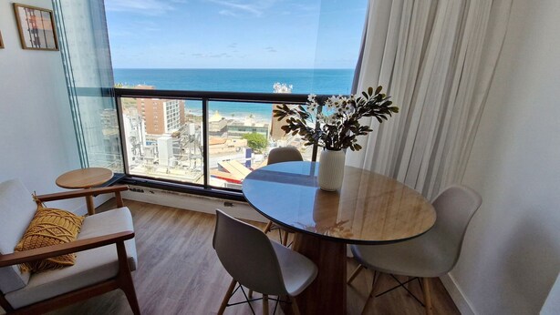 Uma varanda com vista para o mar, uma mesa de jantar com cadeiras e um sofá com manta.
