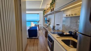 Cozinha moderna com vista para o mar, área de jantar com mesa azul e ilha de cozinha com pia e fogão.