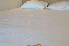 Cama bem arrumada com roupa de cama branca e almofadas, cabeceira de madeira e quarto limpo e sem desordem.