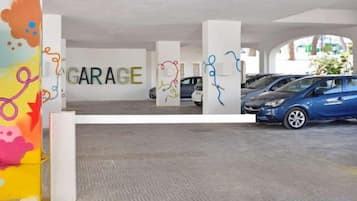 Garagem de estacionamento com vários carros, pilares brancos e uma parede colorida com desenhos abstratos.
