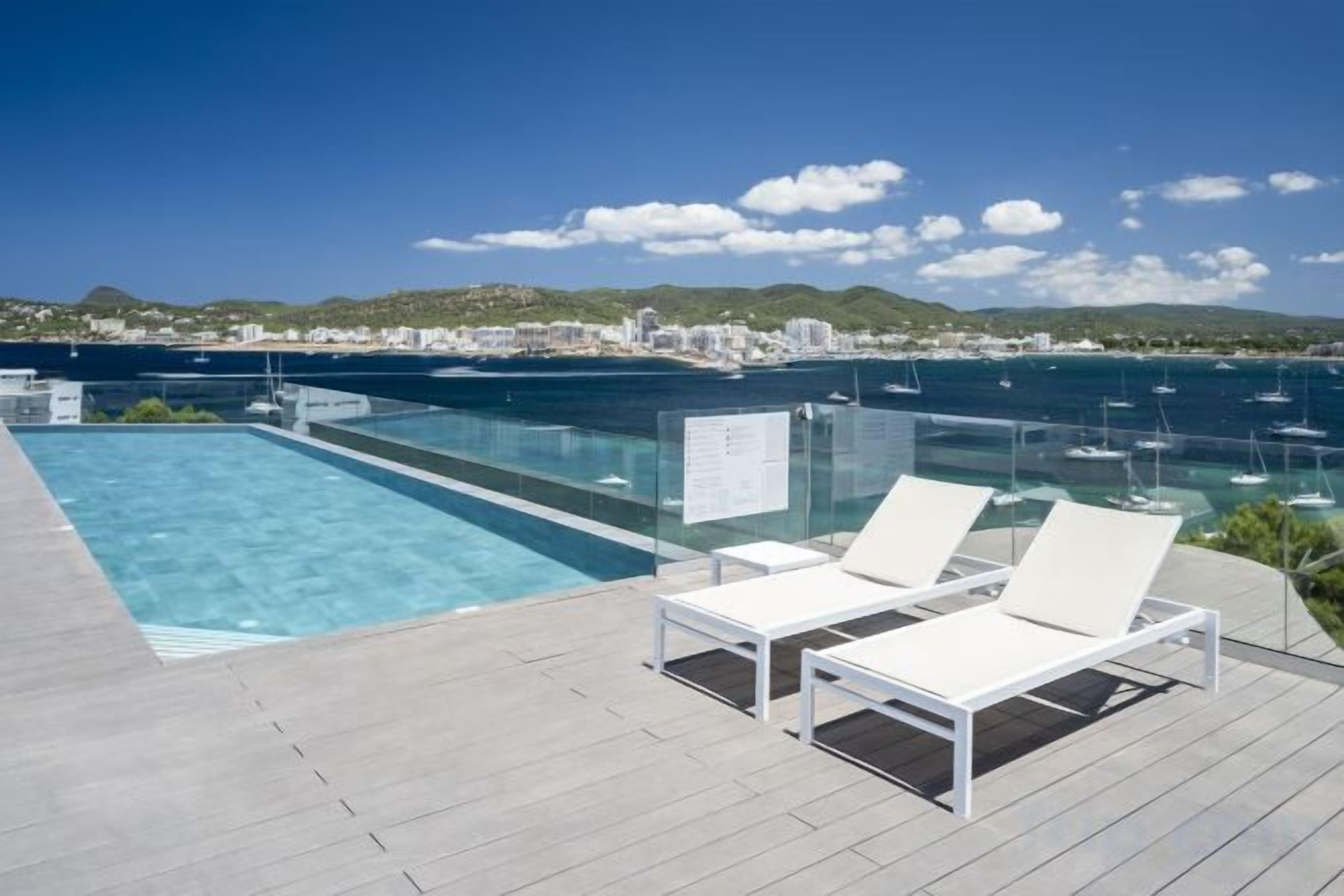 Piscina no terraço com água azul cristalina, com vista para um calhavete com barcos e um horizonte costeiro.