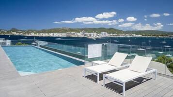 Piscina no terraço com água azul cristalina, com vista para um calhavete com barcos e um horizonte costeiro.