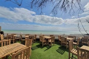 Área externa com mesas e cadeiras, vista para o mar e um cercado branco.