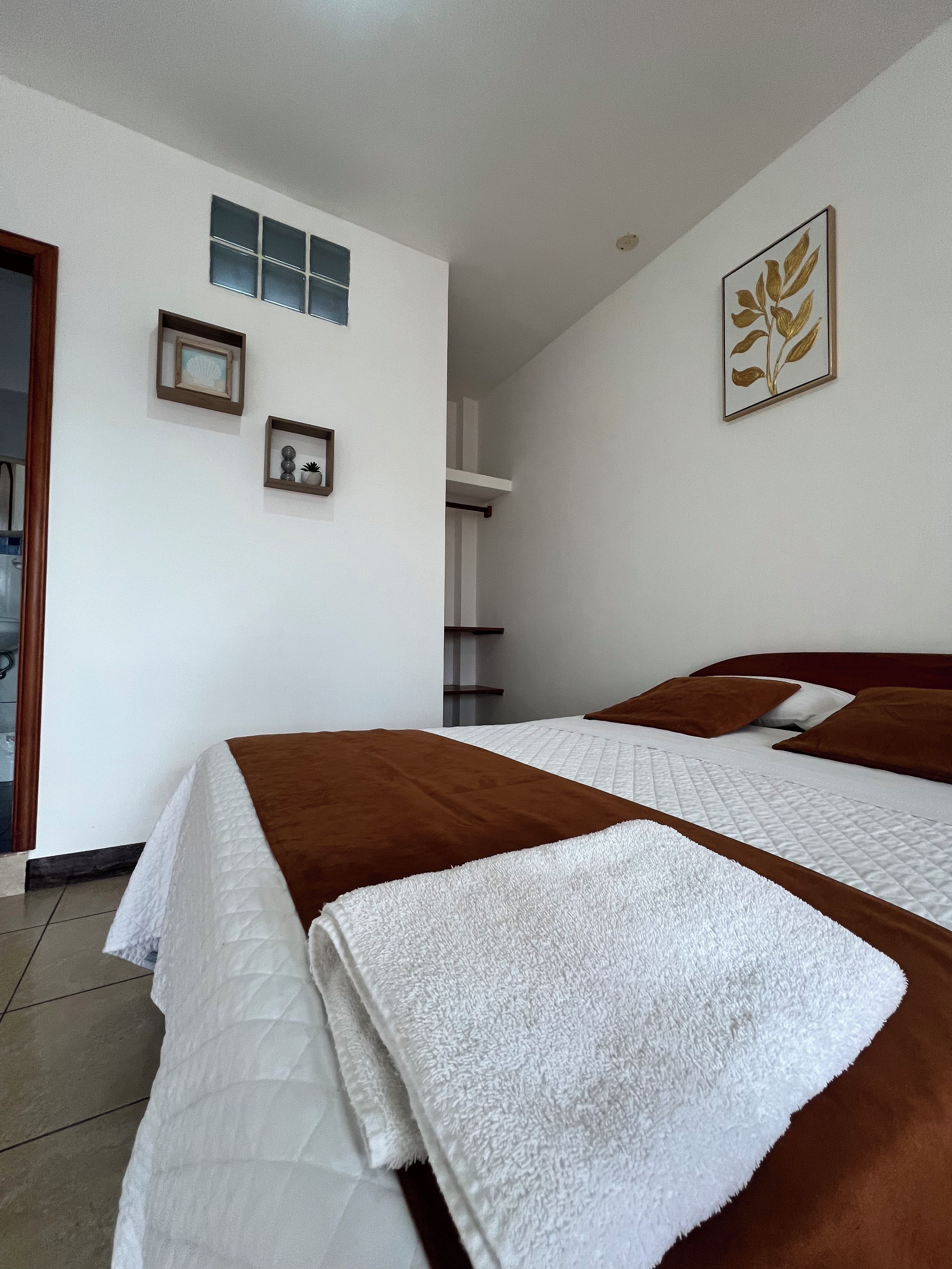 Quarto de hotel com duas camas, parede branca com quadros e uma janela grande.