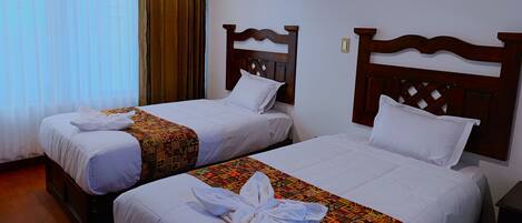 Quarto de hotel com duas camas, cada uma com roupa de cama branca e manta colorida.