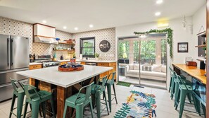 Cozinha moderna com ilha central, área de refeições com cadeiras e vista para o exterior.