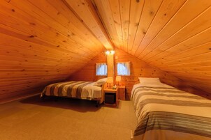 Quarto de sótão aconchegante com duas camas, uma mesa de cabeceira e um abajur.