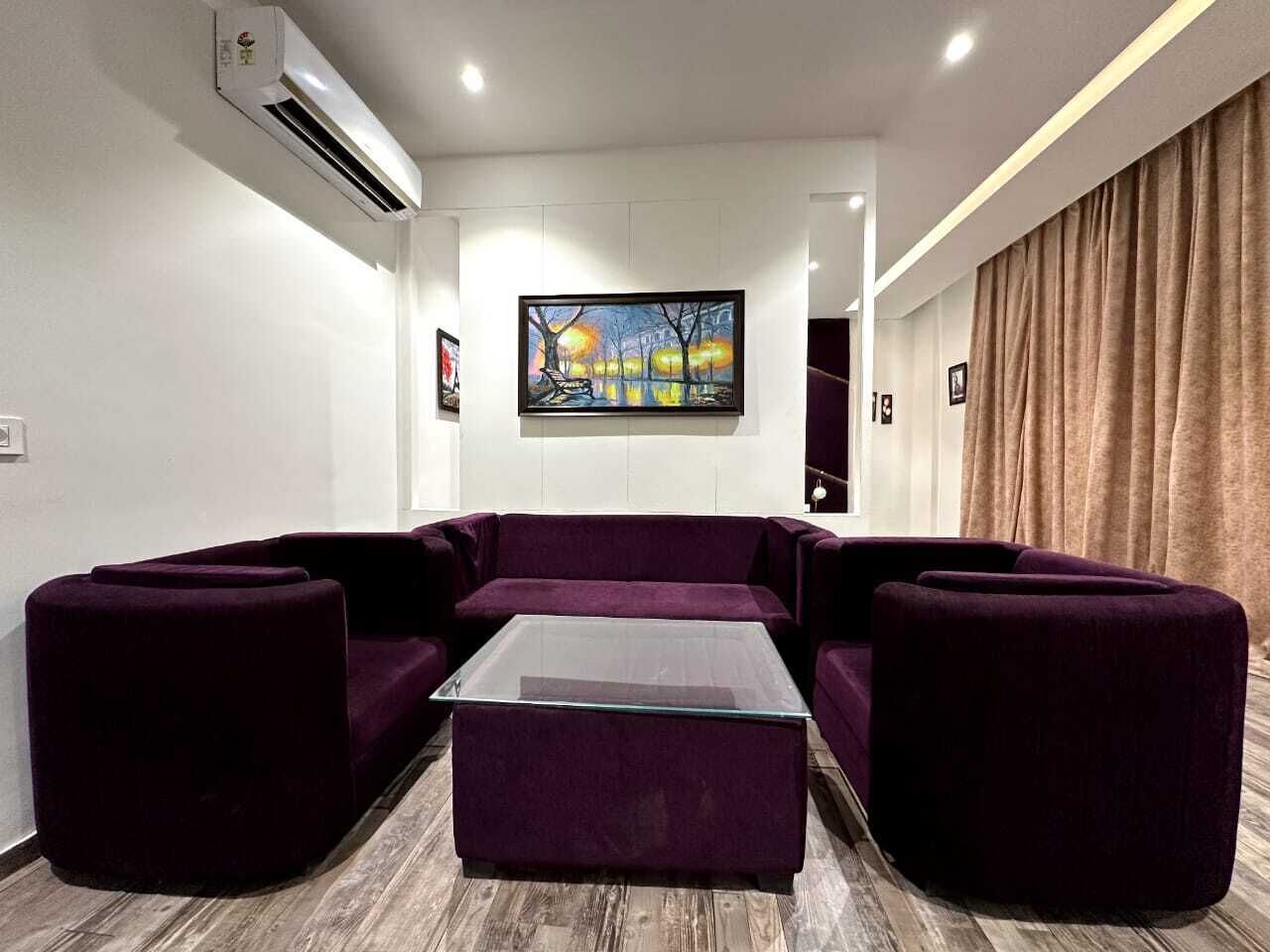 Uma sala de estar moderna com um sofá roxo, uma mesa de centro de vidro e uma pintura na parede.