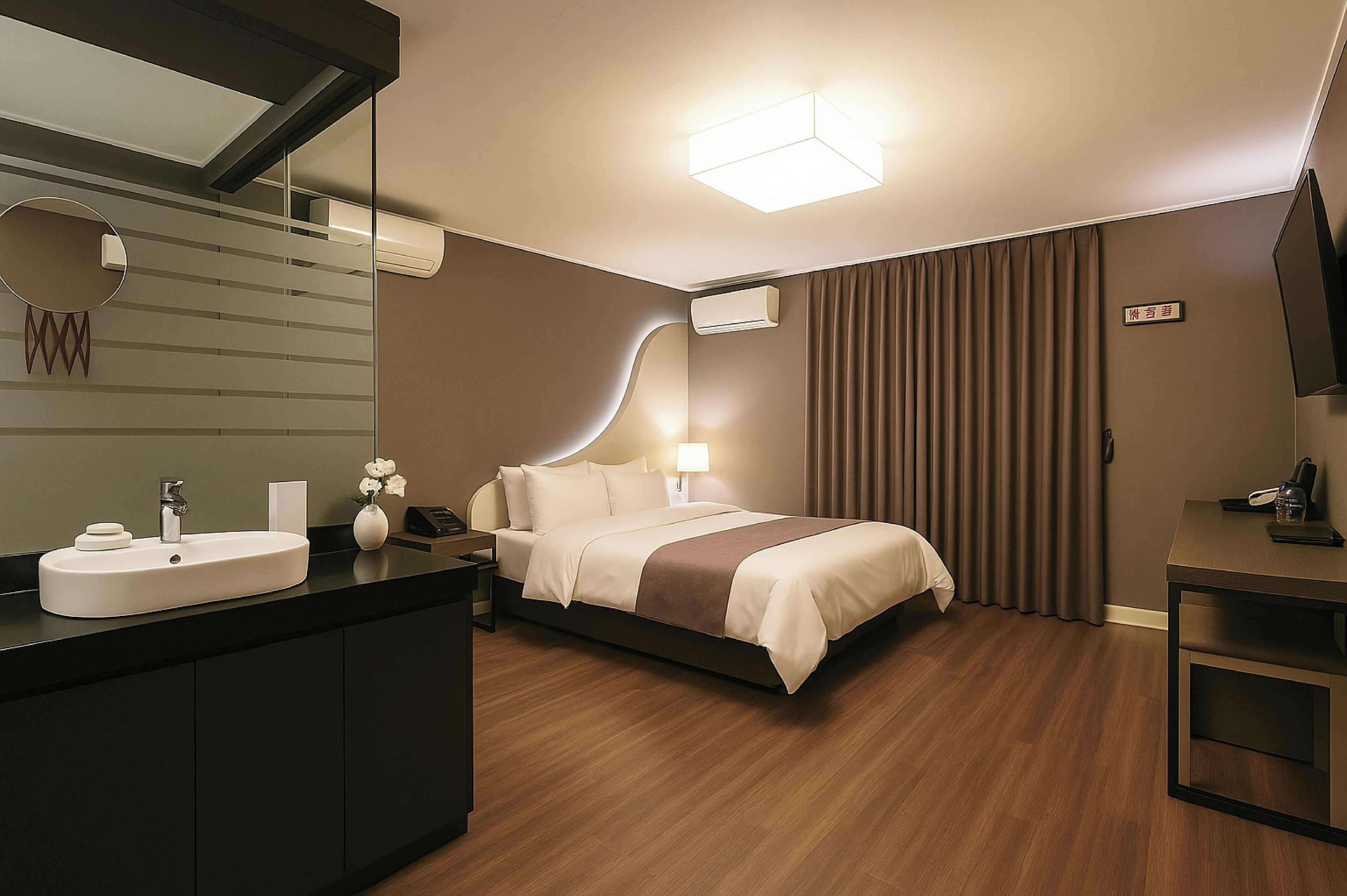Quarto de hotel com cama, mesa de cabeceira, luminária e um espelho grande.