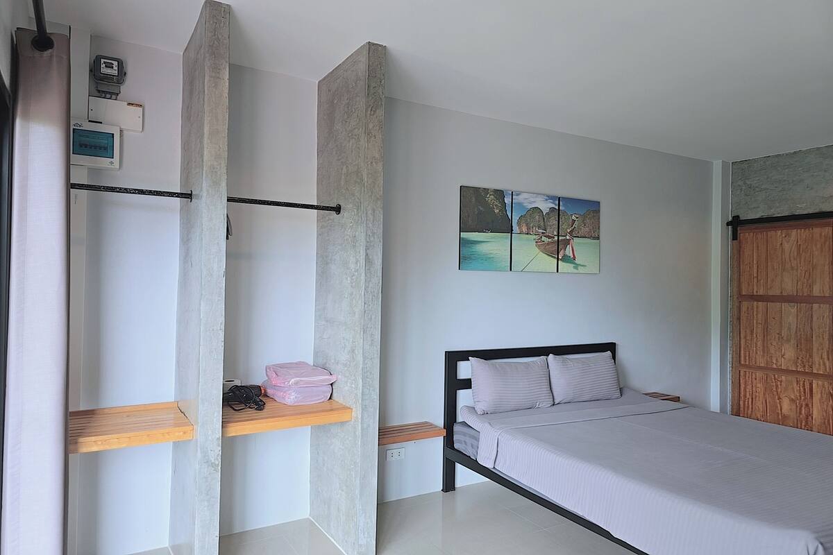 Quarto com cama, prateleira de madeira, um quadro e um guarda-roupa.