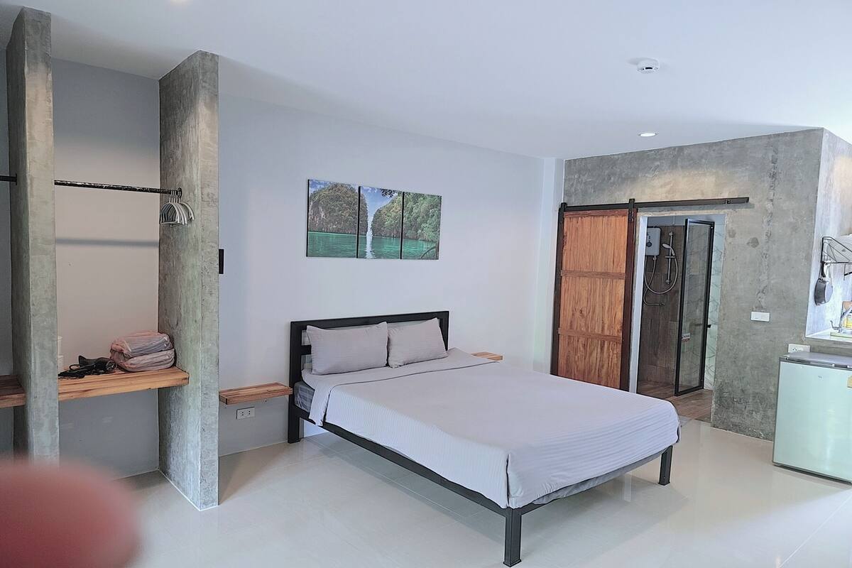 Um quarto moderno com uma cama grande, um banco de madeira e um pilar de concreto.