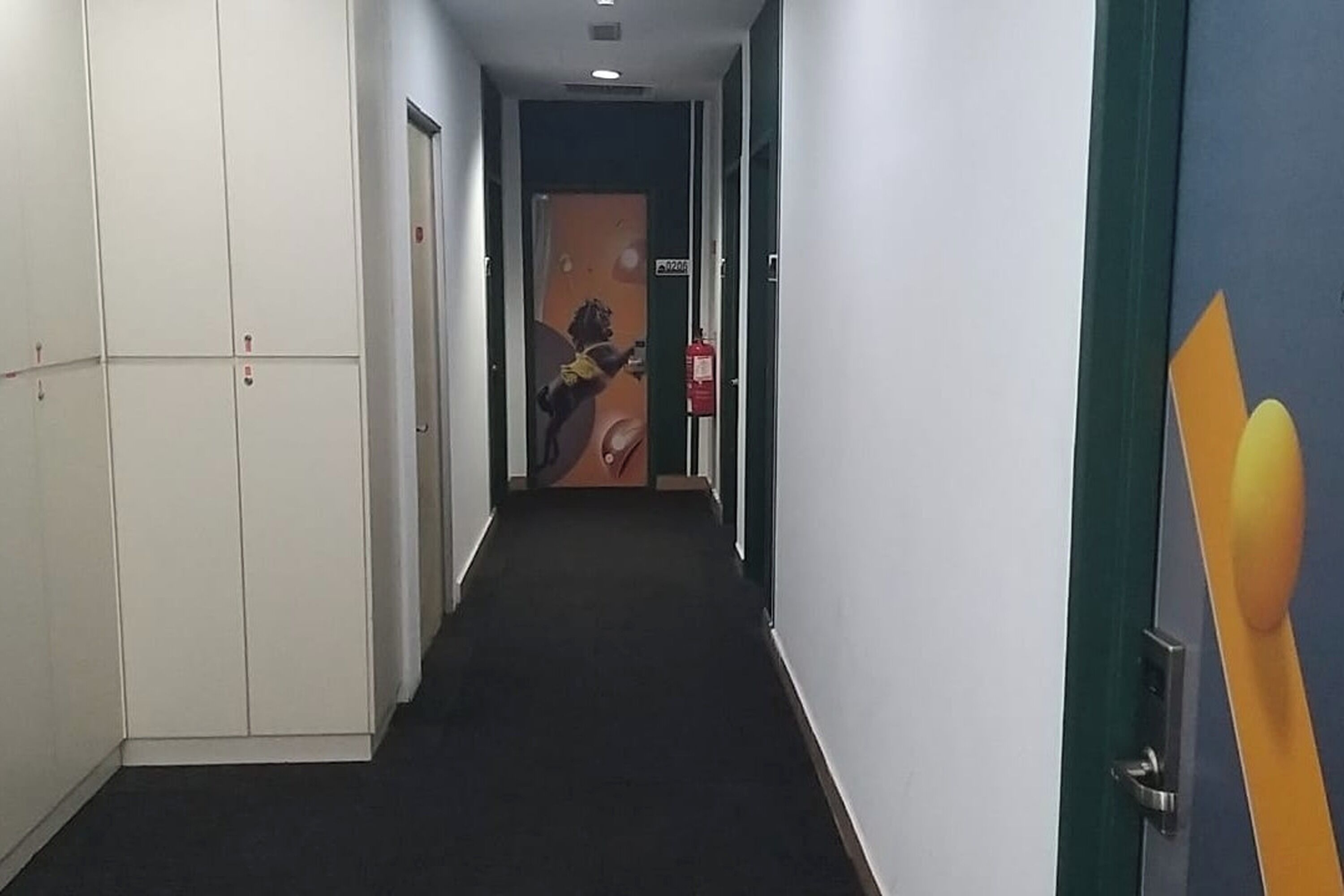 Um corredor com armários de um lado, um extintor de incêndio e uma porta no final.