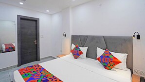 Quarto de hotel moderno com uma cama grande, cabeceira estofada cinza e colcha colorida com padrão geométrico.