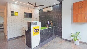 Uma área de recepção de hotel com um balcão, uma TV fixada na parede, um ventilador de teto, um aparelho de ar condicionado e um armário de madeira.