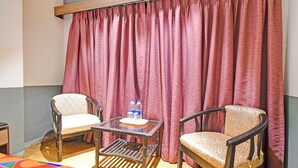 Quarto de hotel com duas cadeiras, uma mesinha com garrafas de água e uma cama.