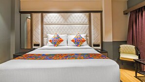 Quarto de hotel com uma cama grande, cabeceira com padrão de losangos, duas almofadas decorativas, mesa de cabeceira, uma cadeira e um espelho na parede.