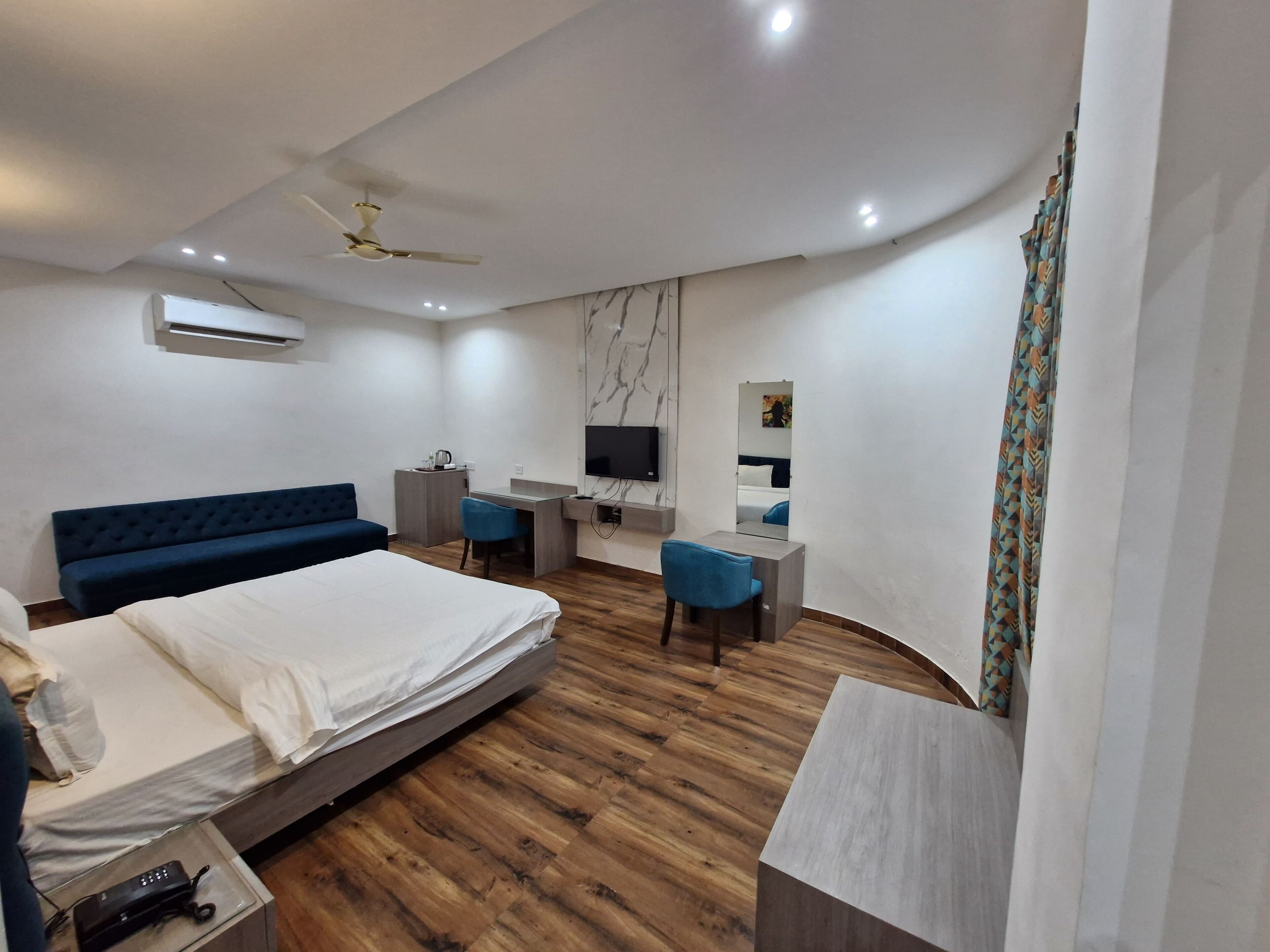 Quarto de hotel moderno com cama, escrivaninha, cadeira, televisão e ventoinha de teto.