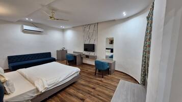 Quarto de hotel moderno com cama, escrivaninha, cadeira, televisão e ventoinha de teto.