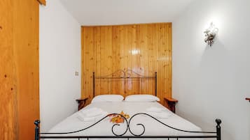 Cama bem arrumada com lençóis brancos e cabeceira decorativa, painéis de madeira na parede e luminária fixada na parede.