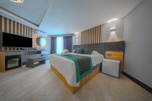 Quarto de hotel moderno com uma cama grande, televisão, escrivaninha e minibar.