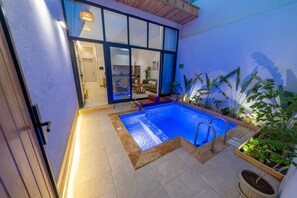 Piscina com deck revestido em azulejos, cercada por plantas em vasos e deck de madeira.
