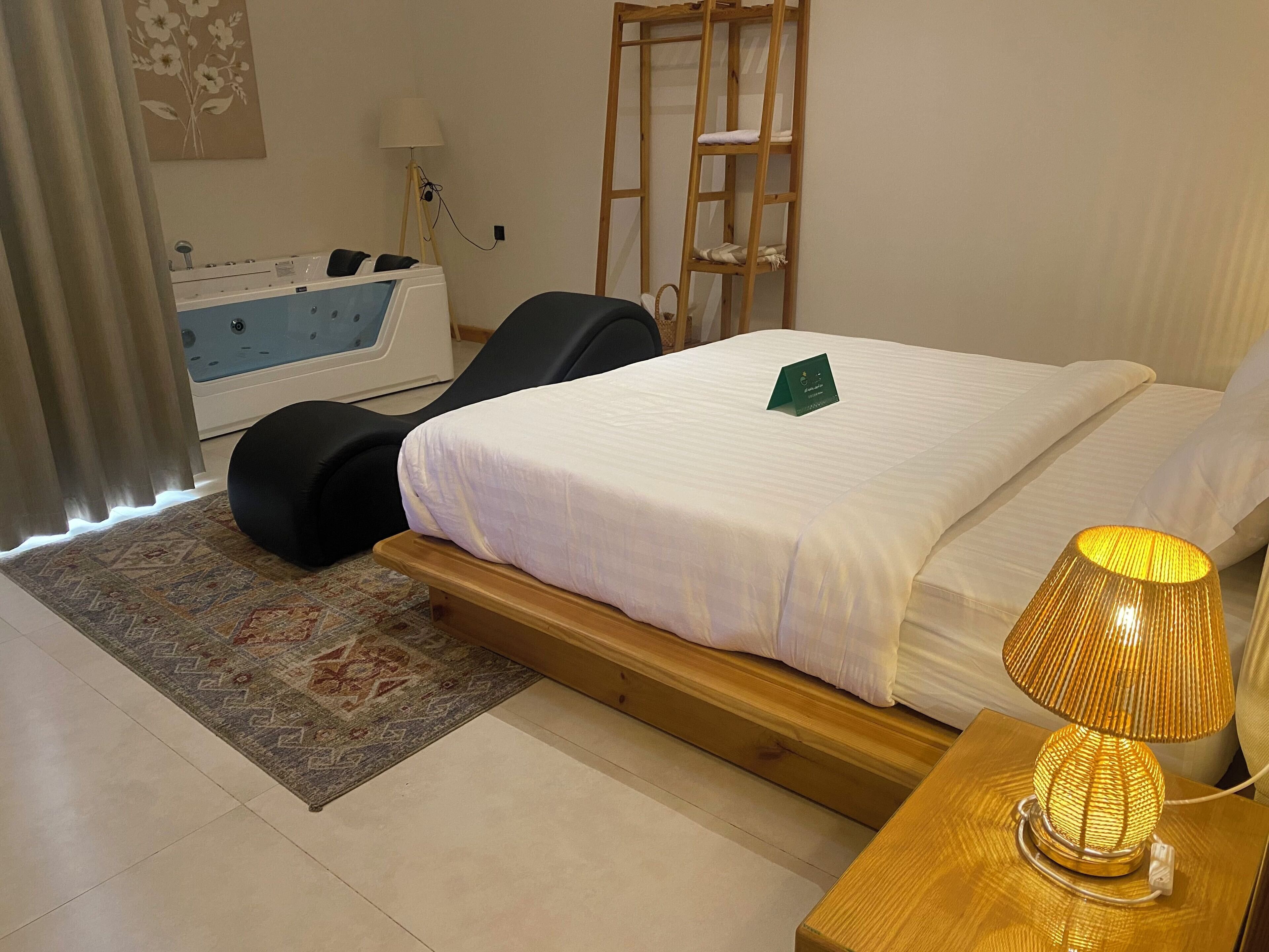 Quarto com cama, cadeira de massagem, escada de madeira, mesa de massagem, luminária e uma pequena placa verde.