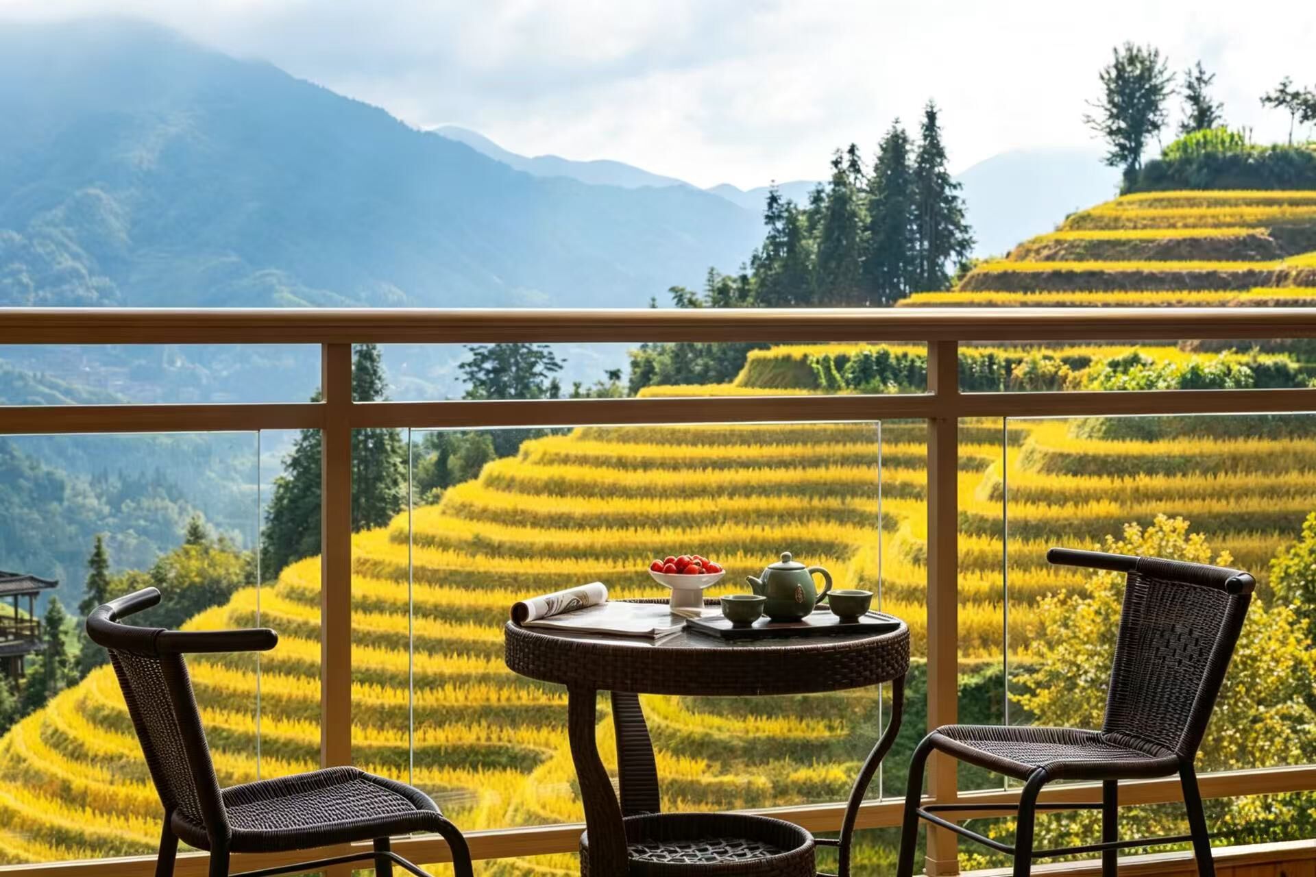 Varanda com mesa e cadeiras, vista para campos amarelados em socalcos e montanhas.