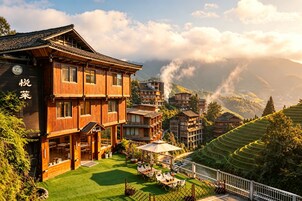 Um edifício de madeira tradicional com terraço, rodeado por campos em socalcos e montanhas.