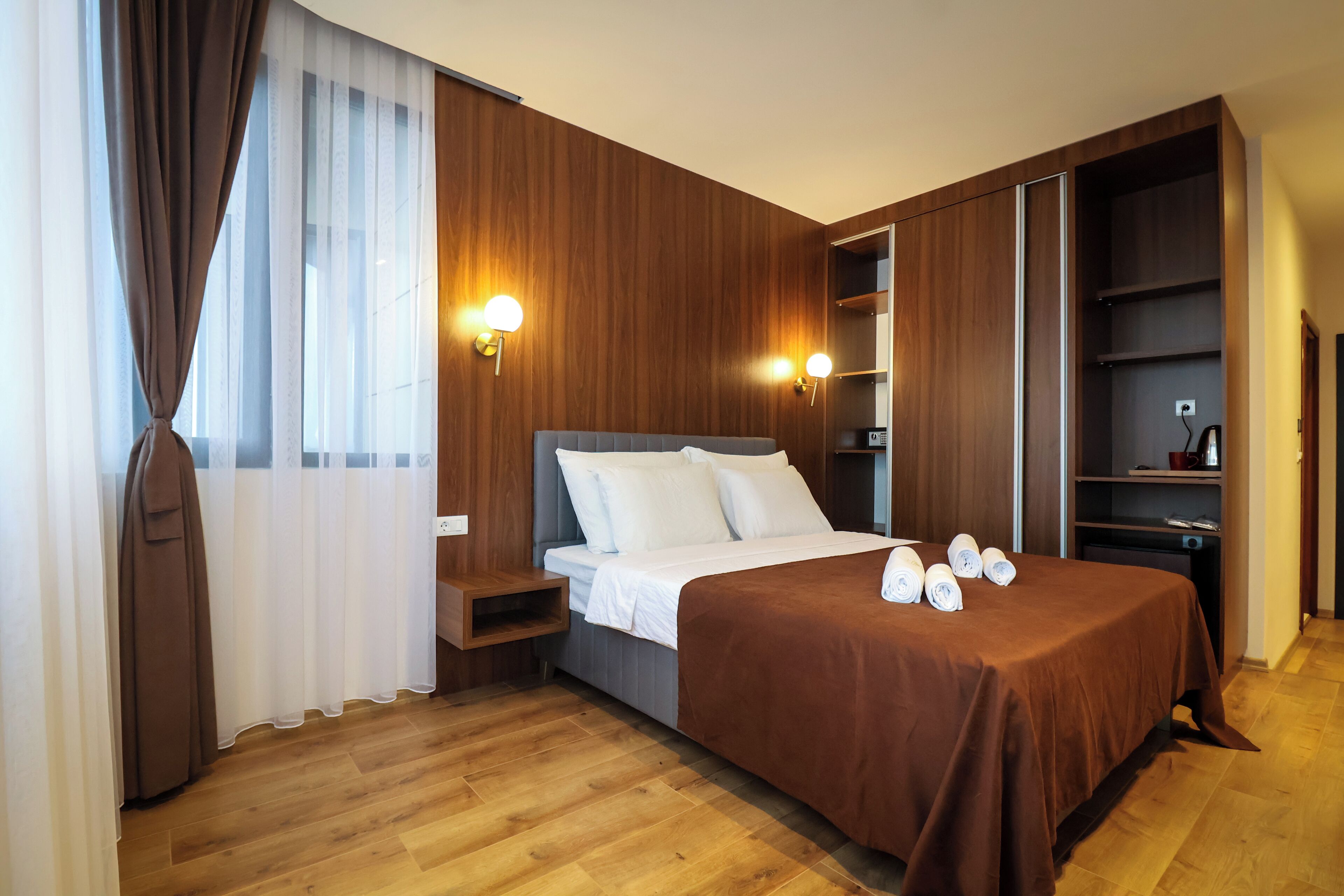 Quarto de hotel moderno com uma cama grande, painéis de madeira, um guarda-roupa e uma mesa de cabeceira.