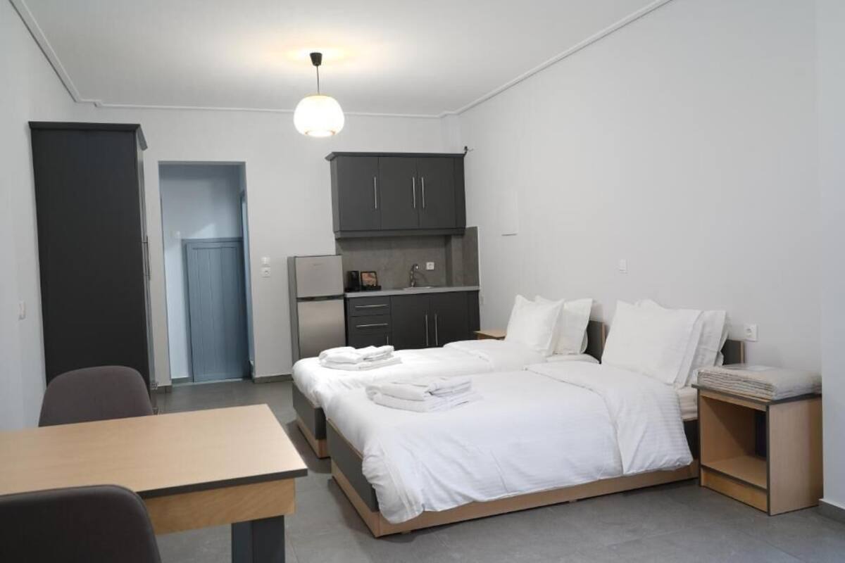 Quarto moderno com cama, mesas de cabeceira, escrivaninha e uma kitchenette.