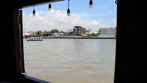 Vista de um quarto com janela para um rio, edifícios e um barco.