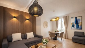 Uma sala de estar moderna com um sofá seccional, uma mesa de centro com um livro, uma área de jantar com mesa e cadeiras, e uma janela grande com cortinas.
