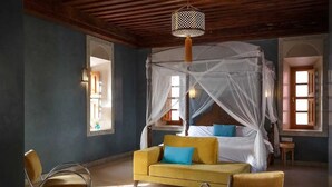 Quarto com cama sob toldo, sofá amarelo e uma cadeira.